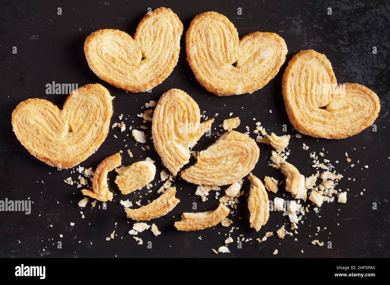 Palmiers, whole and broken puff pastry cookie on old black metal ...