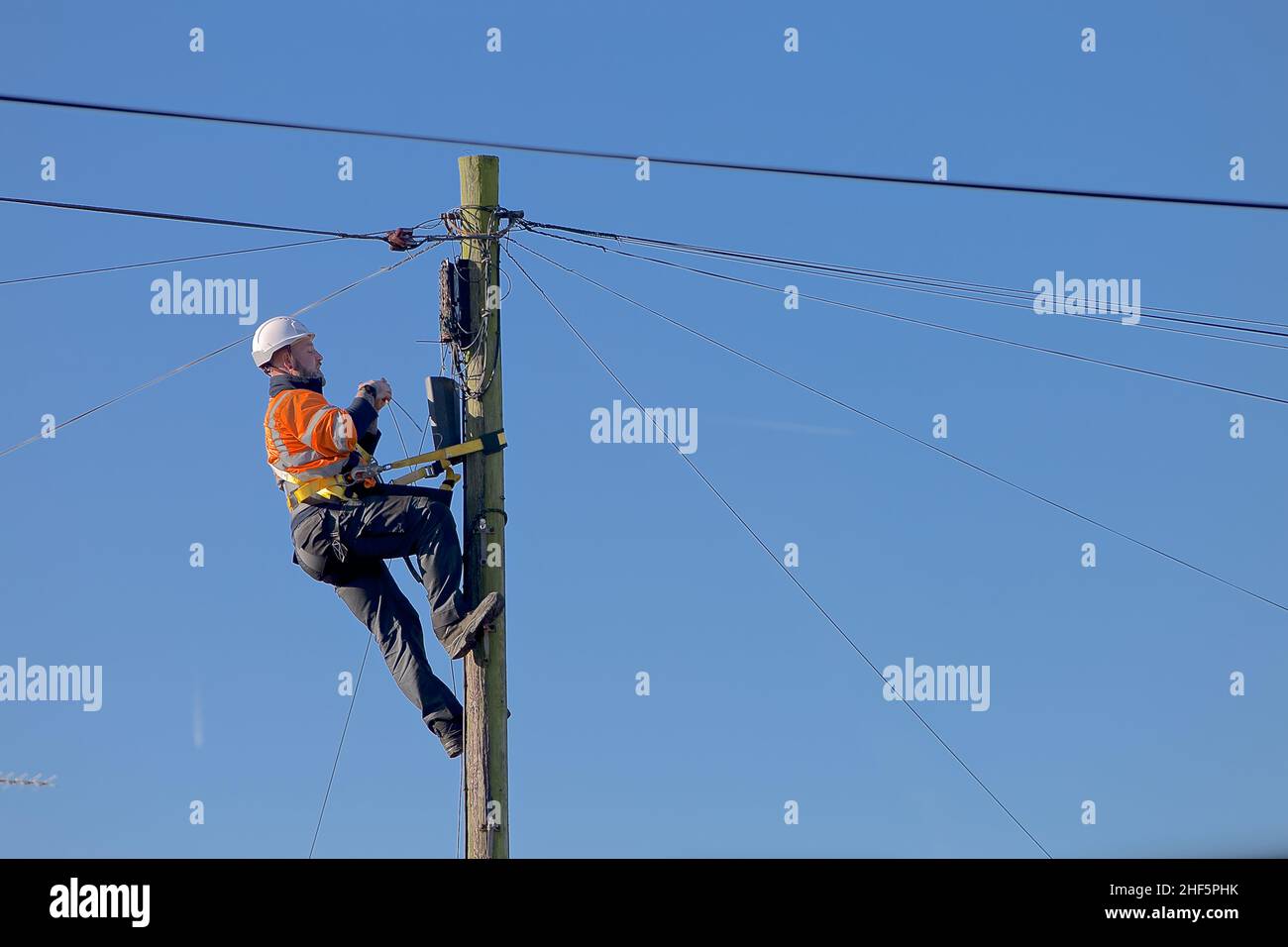 Open reach telecommunications engineer at work up a ladder, he is ...