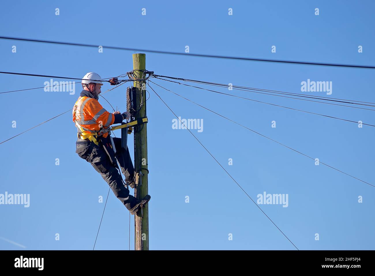 Open reach telecommunications engineer at work up a ladder, he is ...