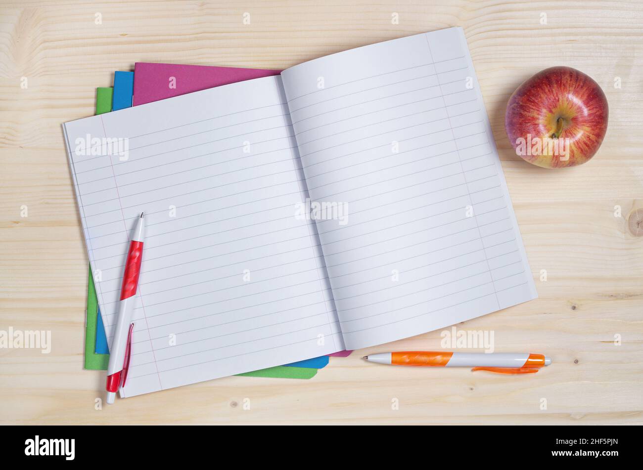 Opened school notebook with pens and apple on the wooden desk. Top view ...