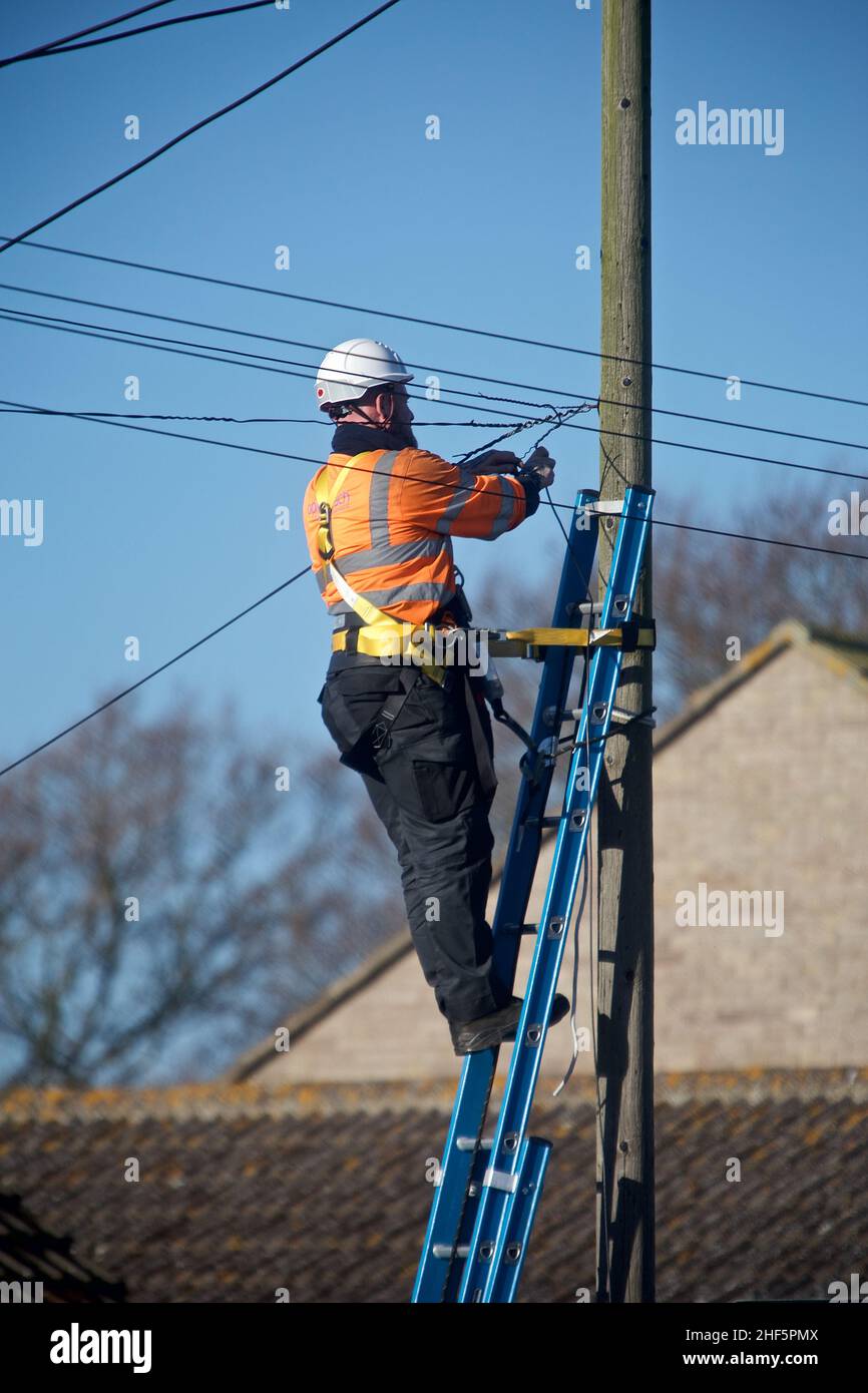 Open reach telecommunications engineer at work up a ladder, he is ...
