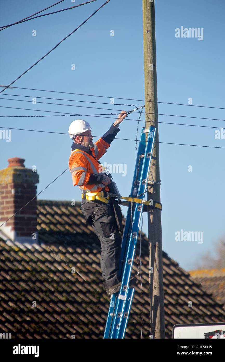 Open reach telecommunications engineer at work up a ladder, he is ...
