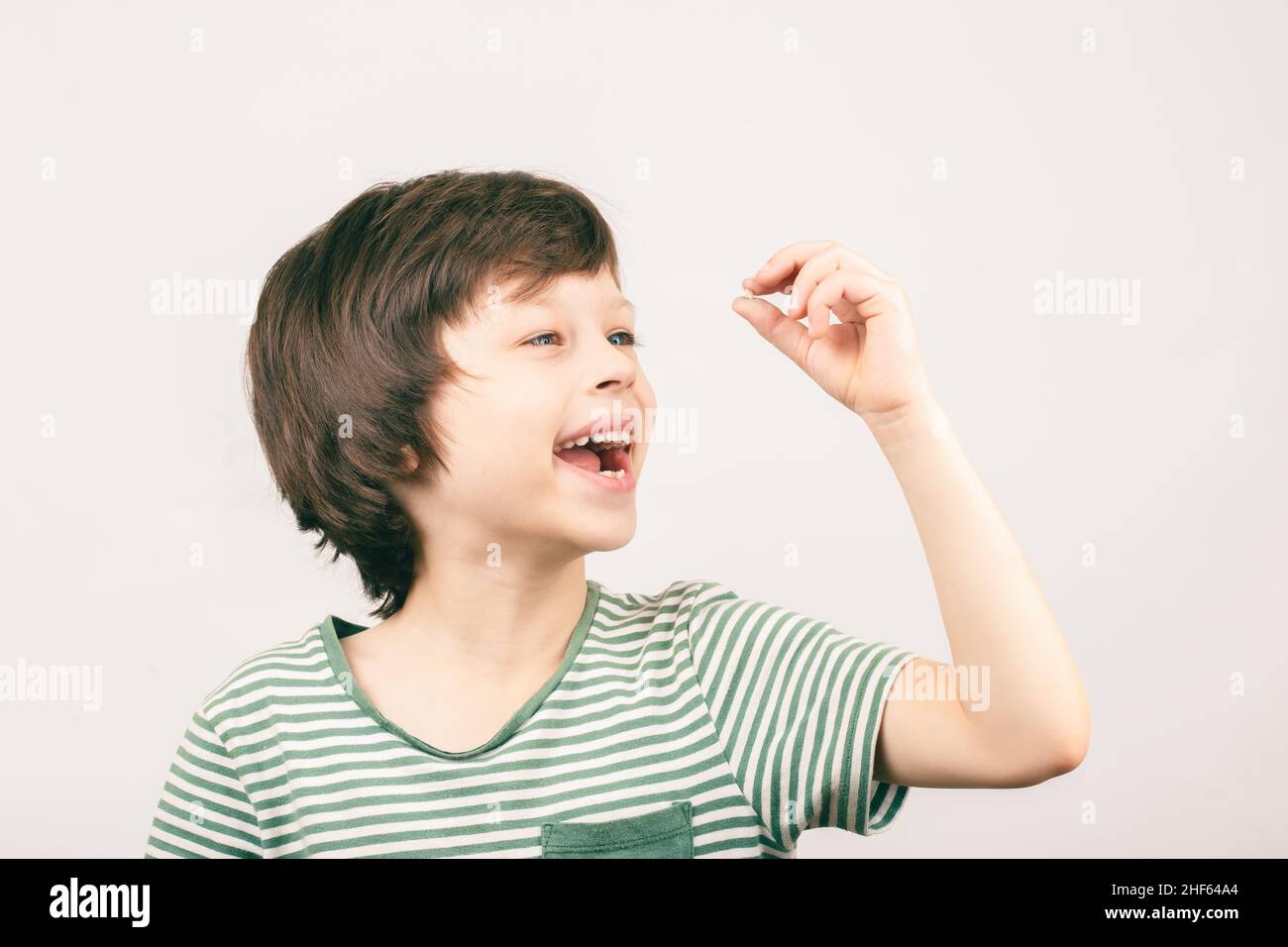 Cheerful boy looking at his first lost bottom front milk tooth over ...