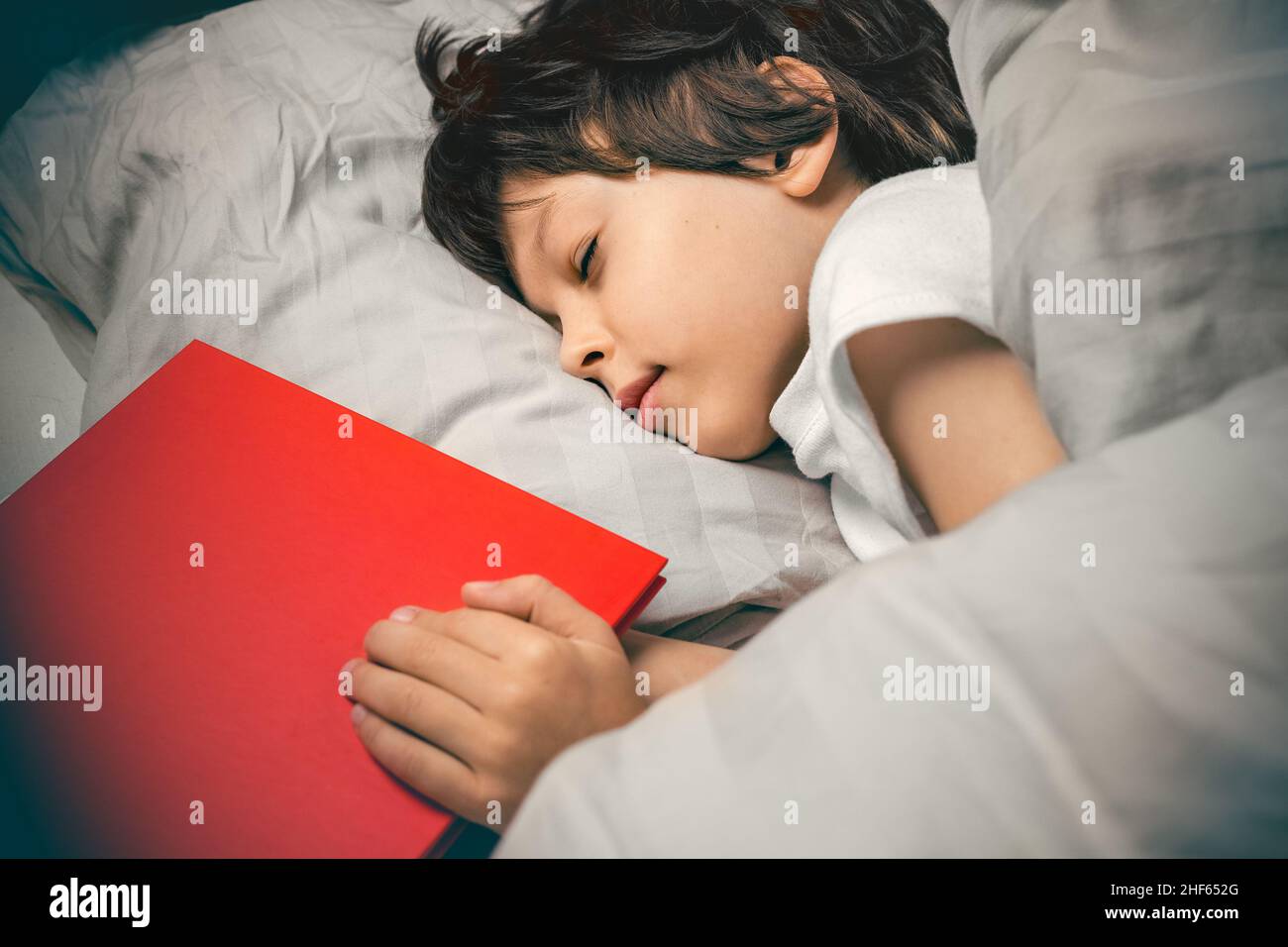 Cute boy peacefully sleeping at night in his bed with a red story book ...