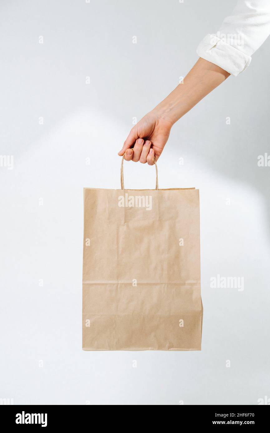 Female hand bringing empty brown paper bag over white background Stock ...