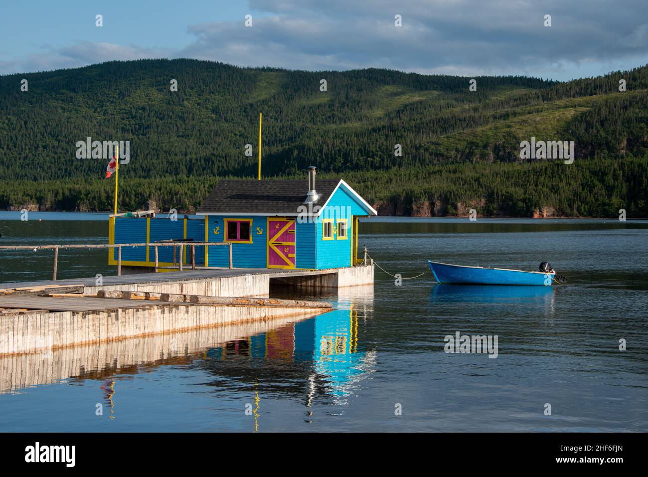 A small boathouse at the end of a wooden pier. The bright teal blue ...