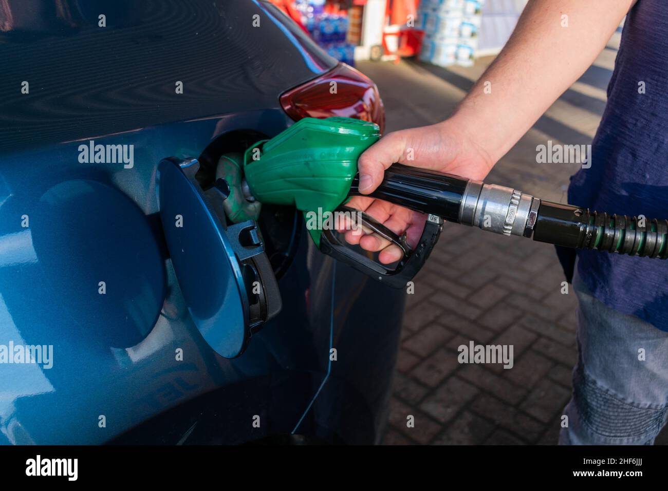 Man holding petrol nozzle pump filling up blue car at a gas station ...