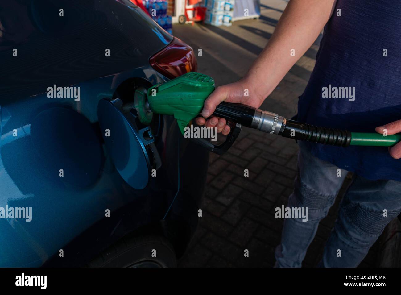 Man holding petrol nozzle pump filling up blue car at a gas station ...