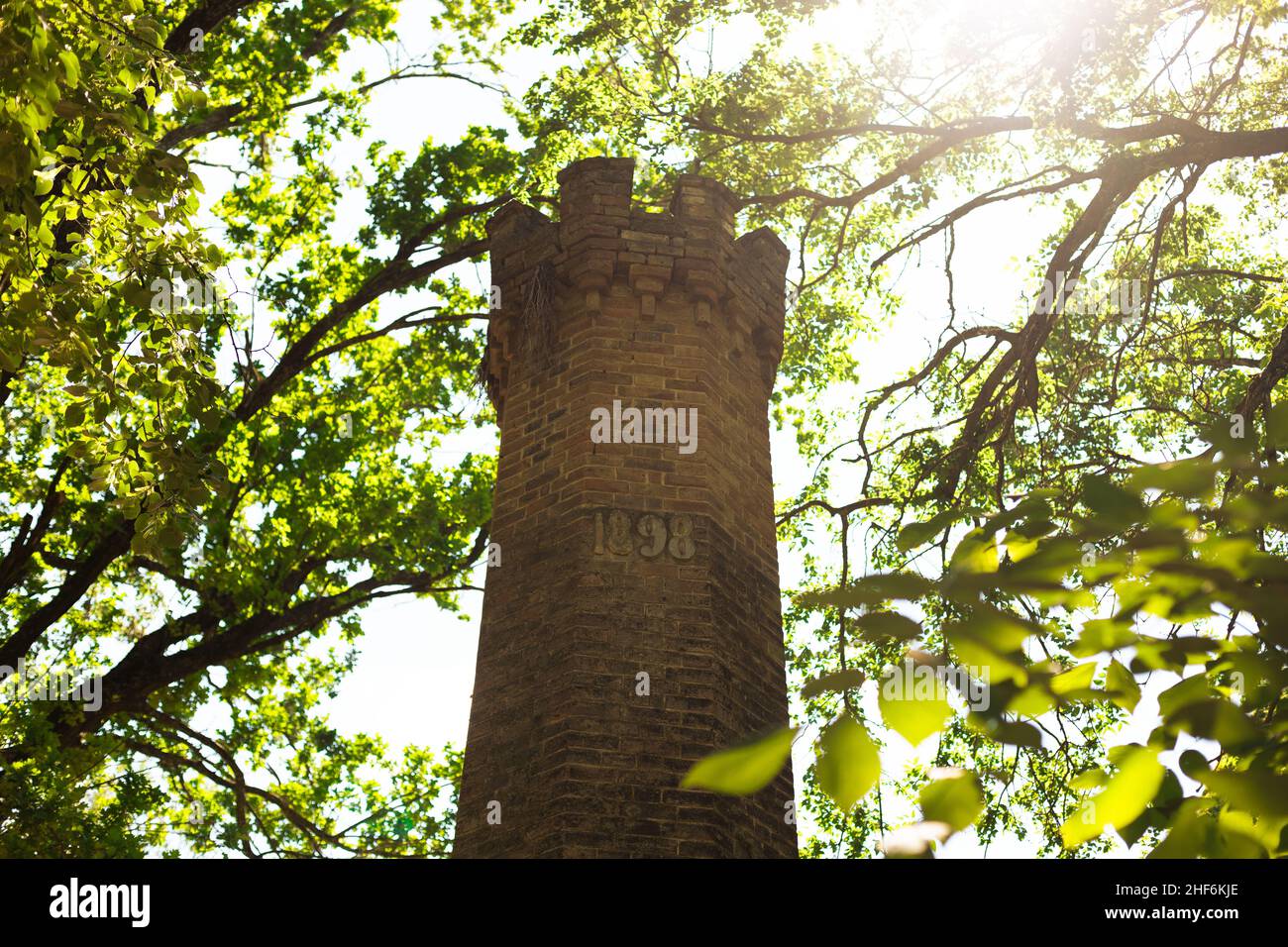 Old brick tower with green tree branches in city park on blue sky ...
