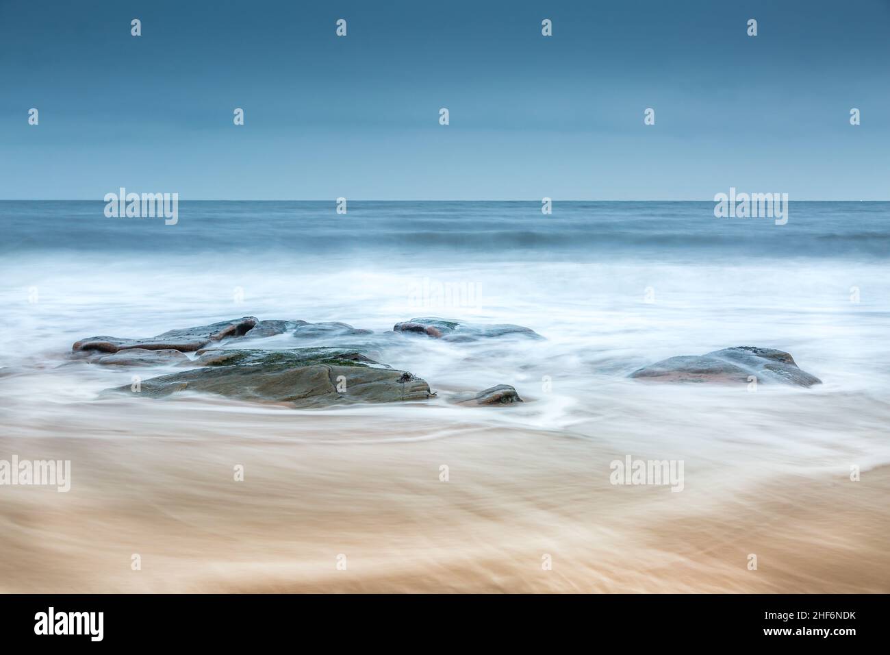 A cluster of rocks on the beach as the wave backwash returns to the sea ...
