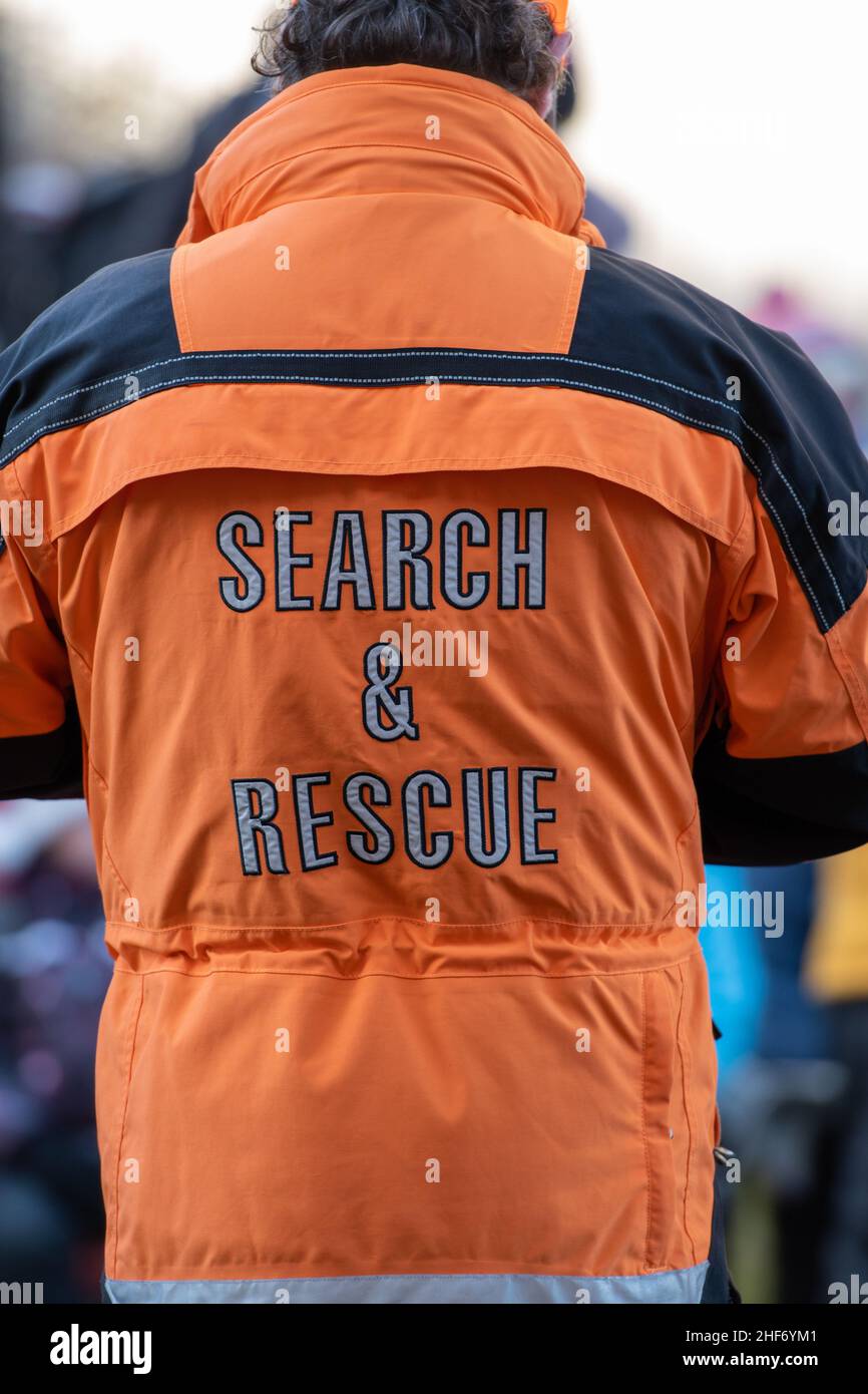 A male adult stands among a crowd wearing a bright orange vest with the ...