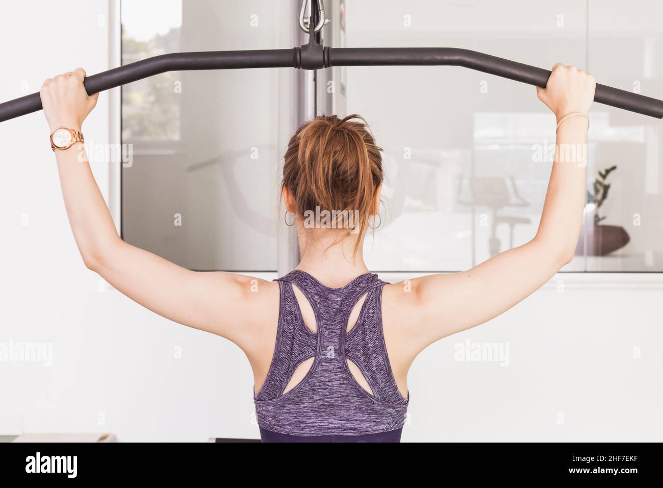 Young blond sporty girl does machine lat pulldown back exercise in a ...