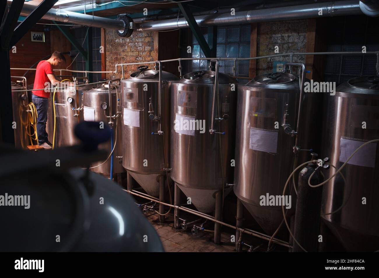 Brewery worker cleaning beer tanks, using water hose to wash inside ...
