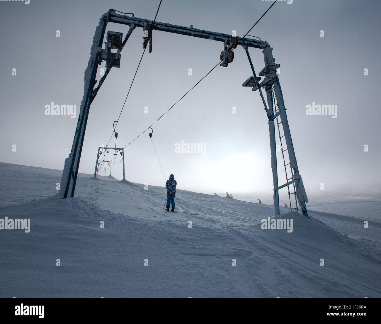 Ski lift at the top in the snowy mountains lifts a person up the slope ...
