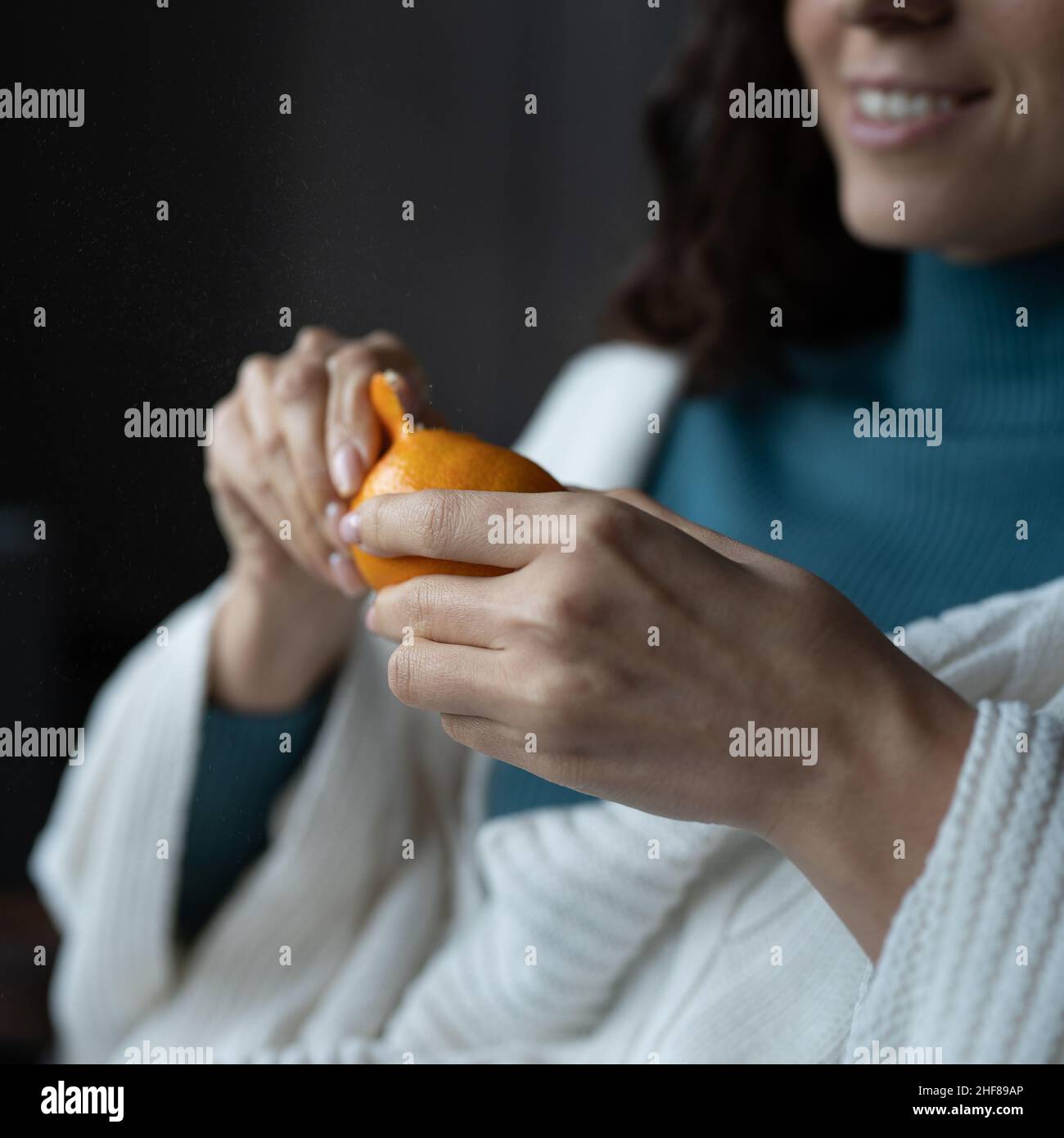 Smiling young woman peels juicy ripe tangerine, home eating seasonal ...