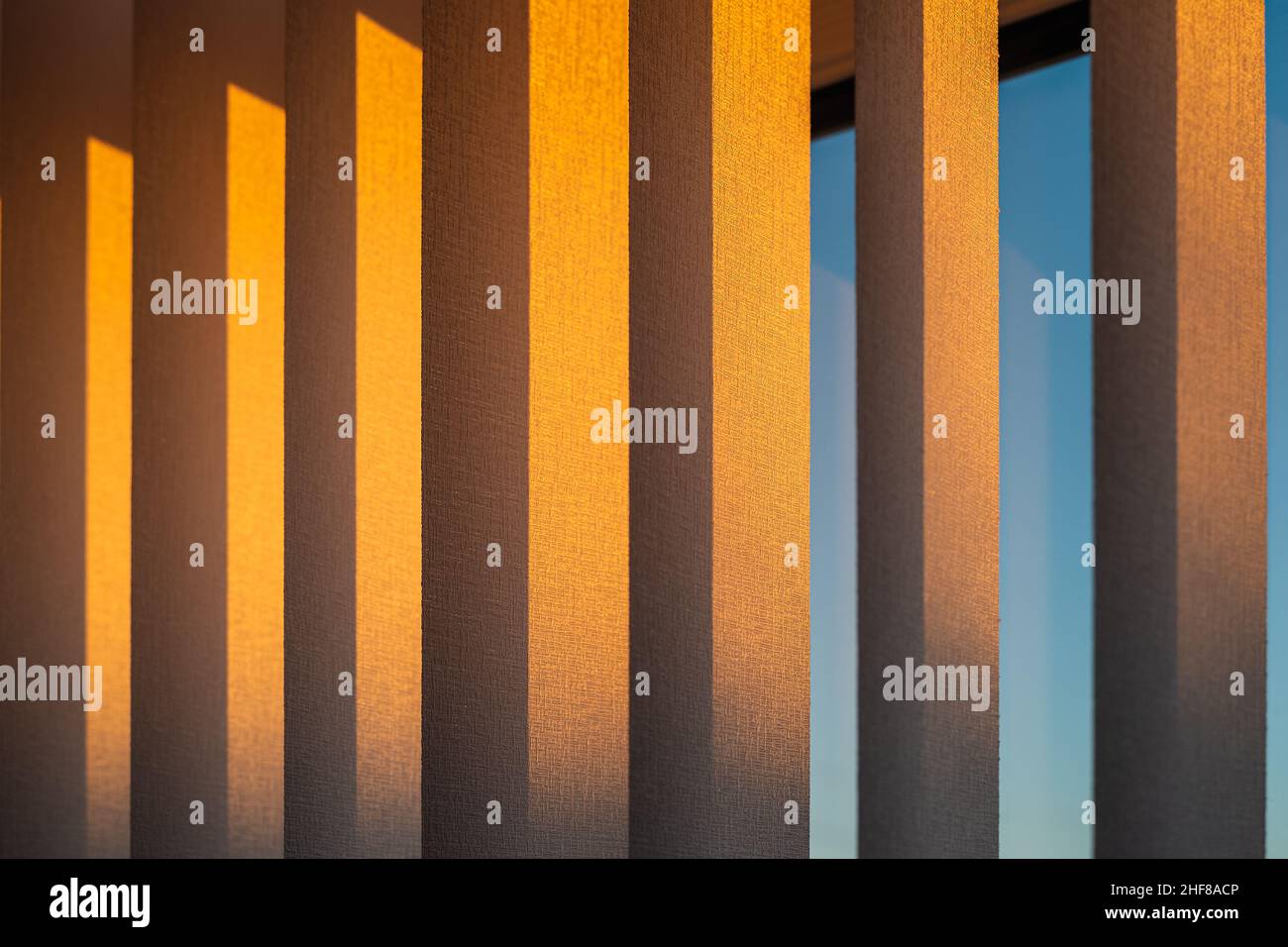 Hanging white textured vertical window slats reflecting the gold of a ...