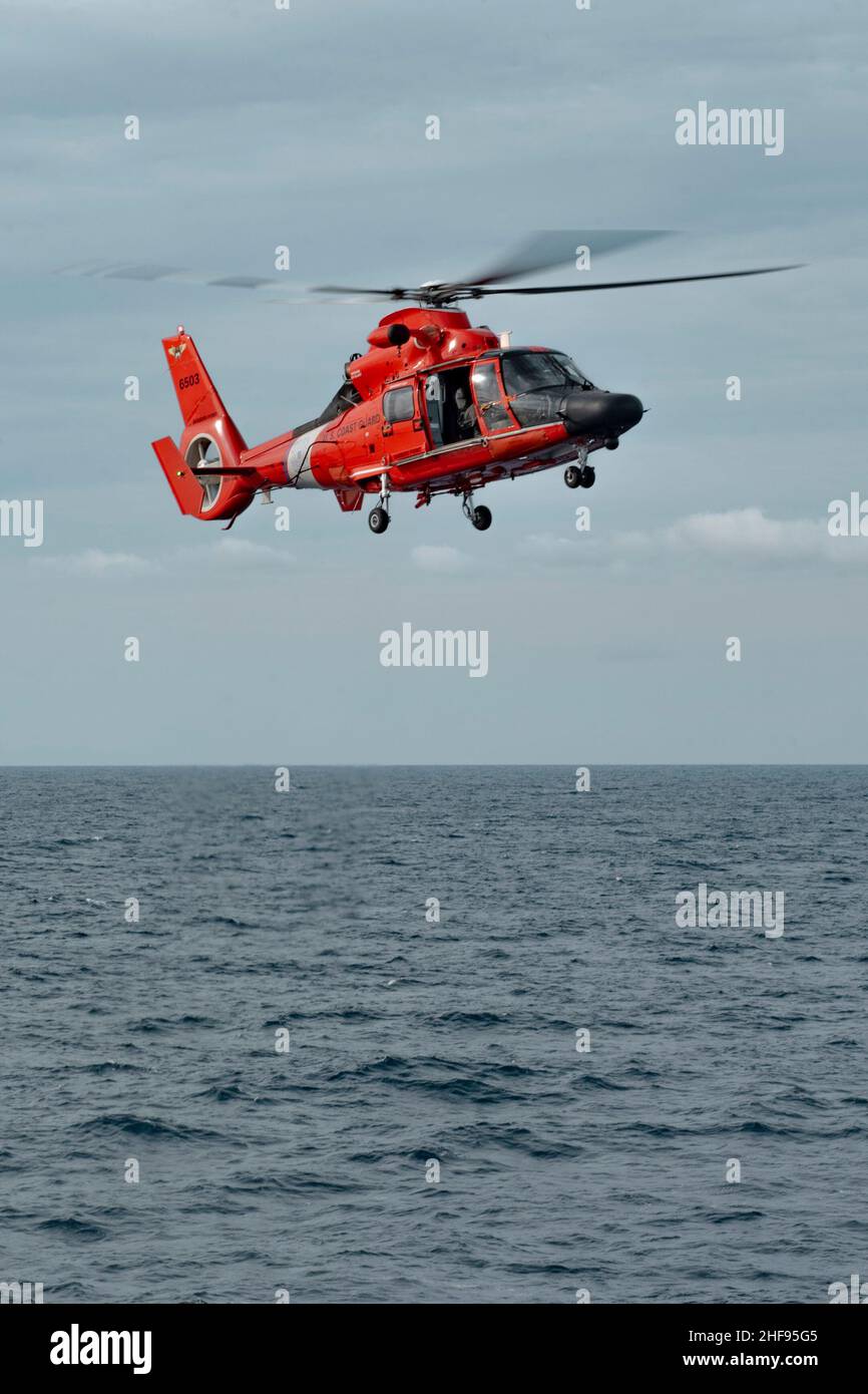 A U.S. Coast Guard MH-65E Dolphin helicopter flies along the USCGC ...