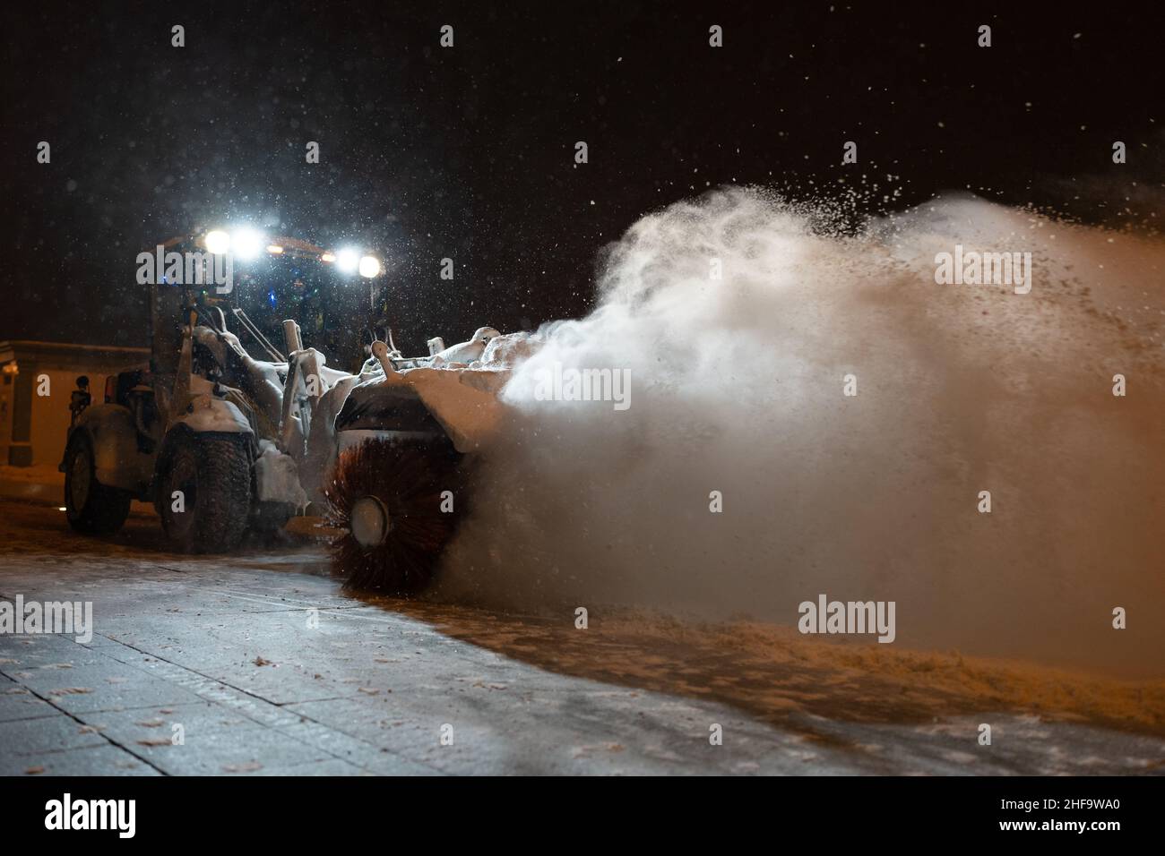 Yellow tractor with rotary sweeper clearing city streets at night in ...