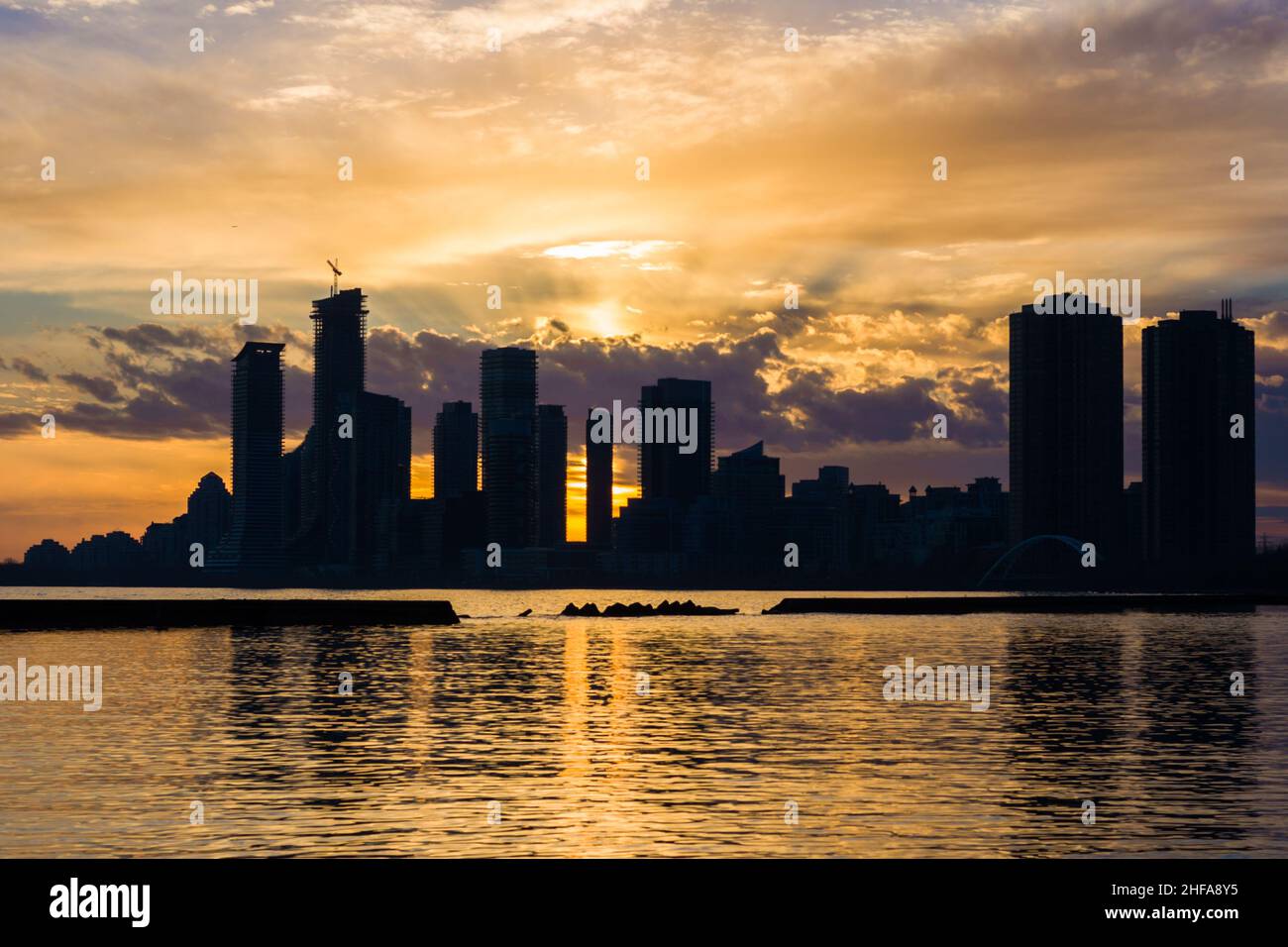 Amazing sunset over sityscape. Cloudy sky with sun rays, lake water ...