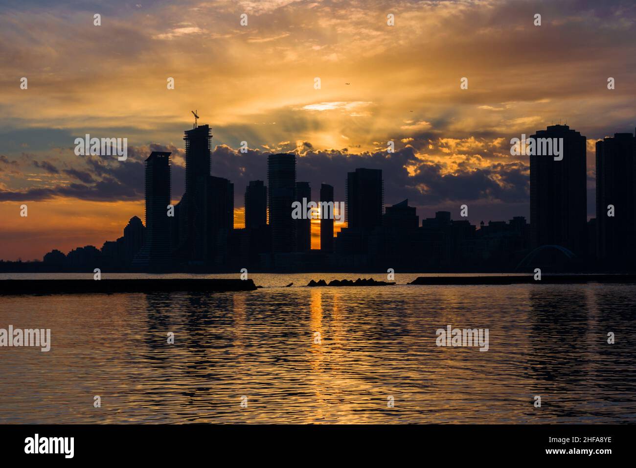 Amazing sunset over sityscape. Cloudy sky with sun rays, lake water ...
