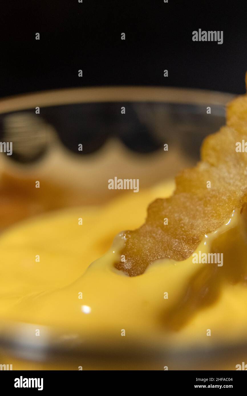 Wavy French fry being dipped into melted cheese Stock Photo - Alamy