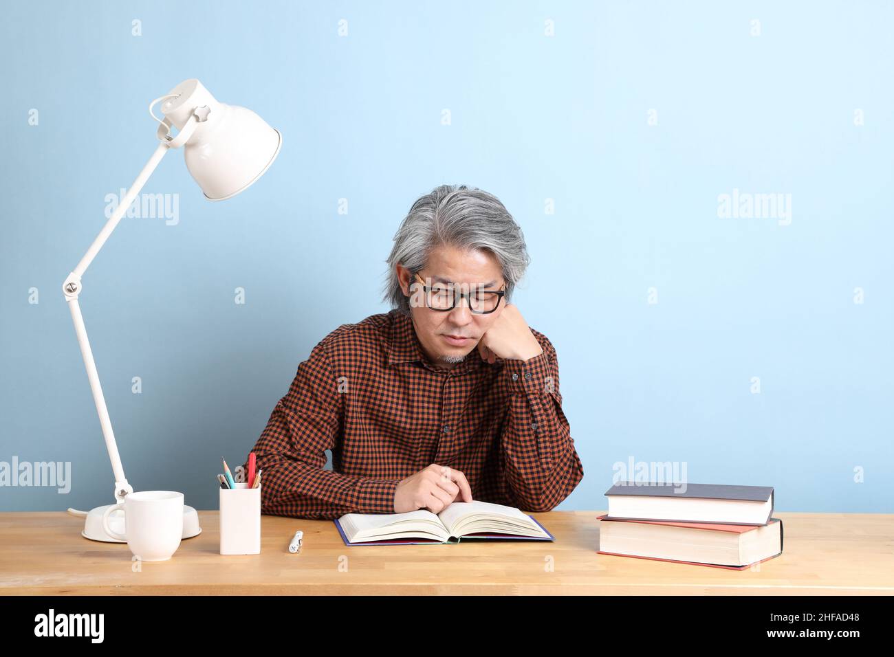 The senior Asian man reading the books at the desk with the blue ...
