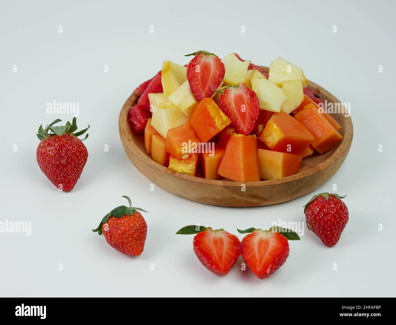 sliced strawberry, papaya, apple, and watermelon on a wooden plate on ...