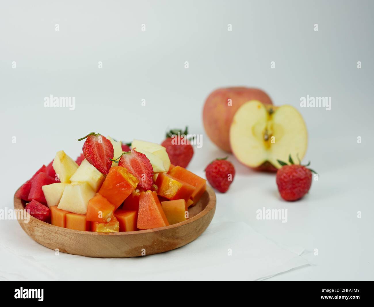 sliced strawberry, papaya, apple, and watermelon on a wooden plate on ...