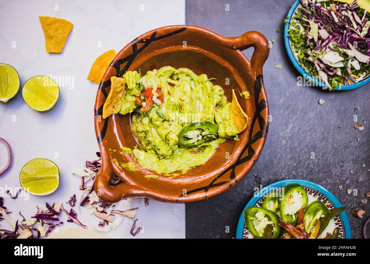 Delicious spicy guacamole in traditional clay pot above black and white ...
