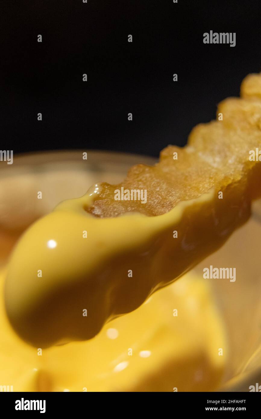 Wavy French fry being dipped into melted cheese Stock Photo - Alamy