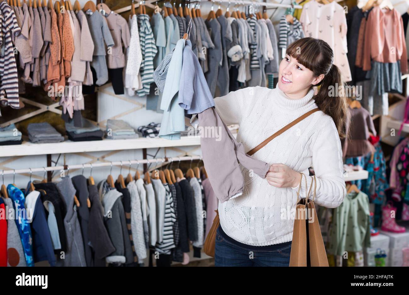 Pregnant woman deciding on clothes for baby in children’s clothes shop ...