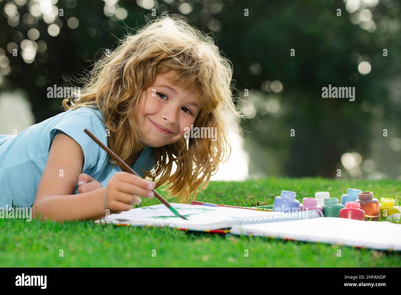 Kids drawing. Child boy draws in park laying in grass having fun on ...