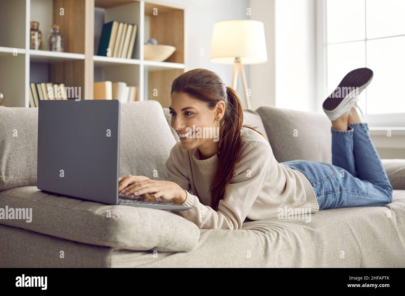 Happy woman lying on a comfy sofa and using her laptop computer for ...