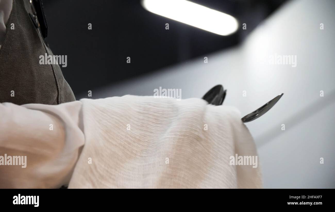 Close up of hands wiping cutlery with a piece of white clean cloth. A ...