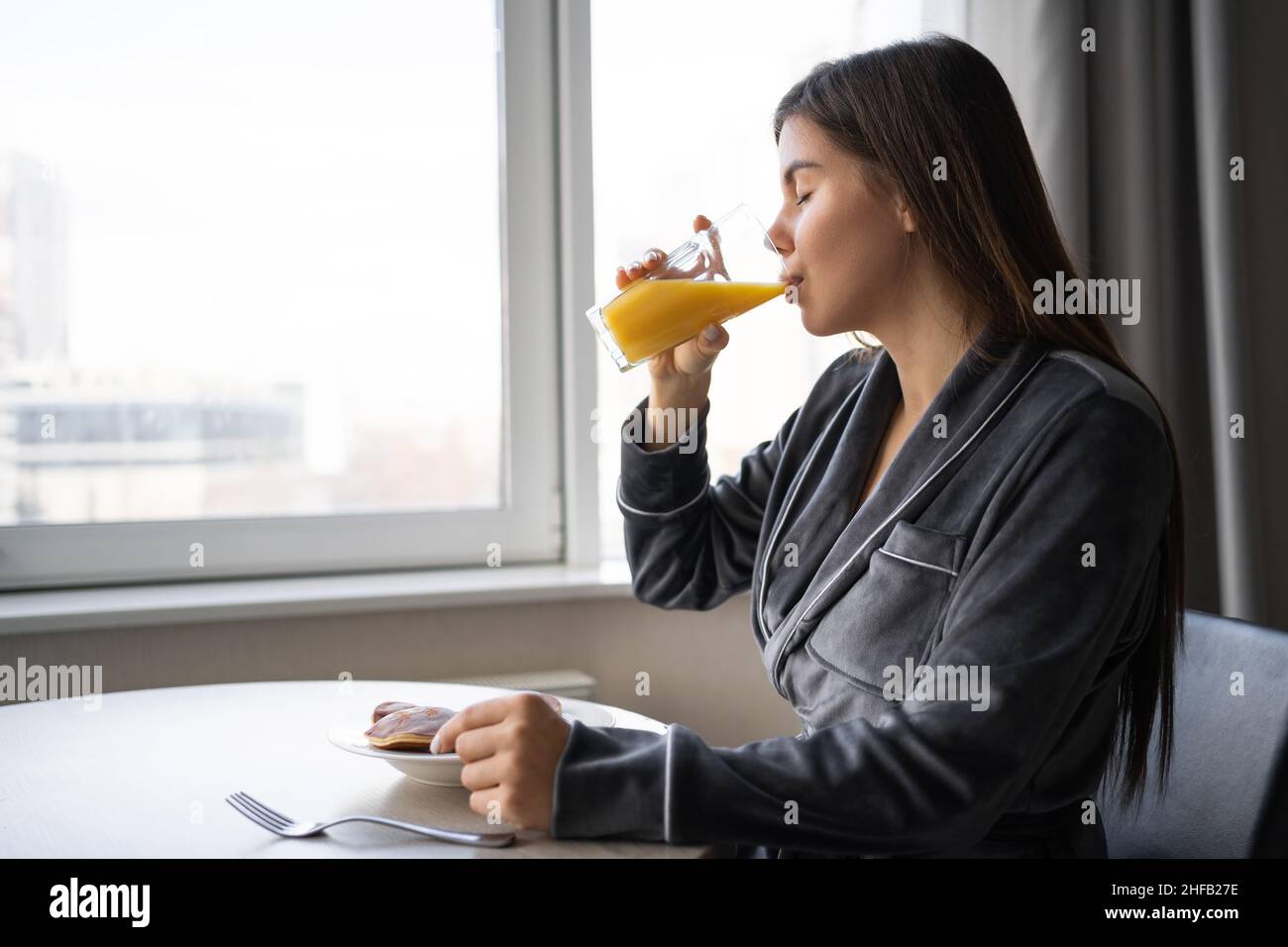 Young woman enjoying fresh orange juice. In her kitchen, the lady is ...