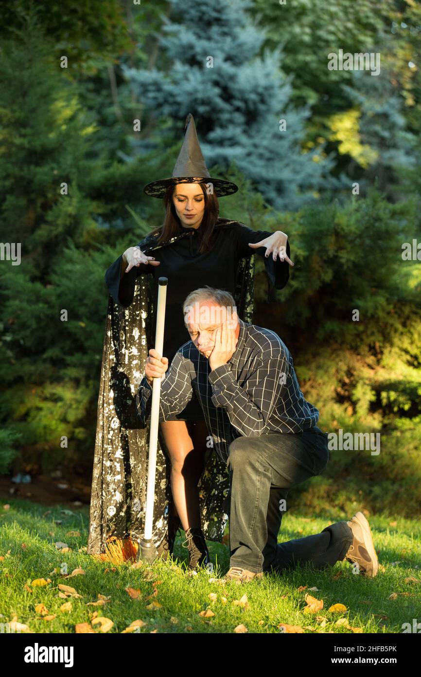 A young beautiful girl in a witch's costume is trying to bewitch a man ...