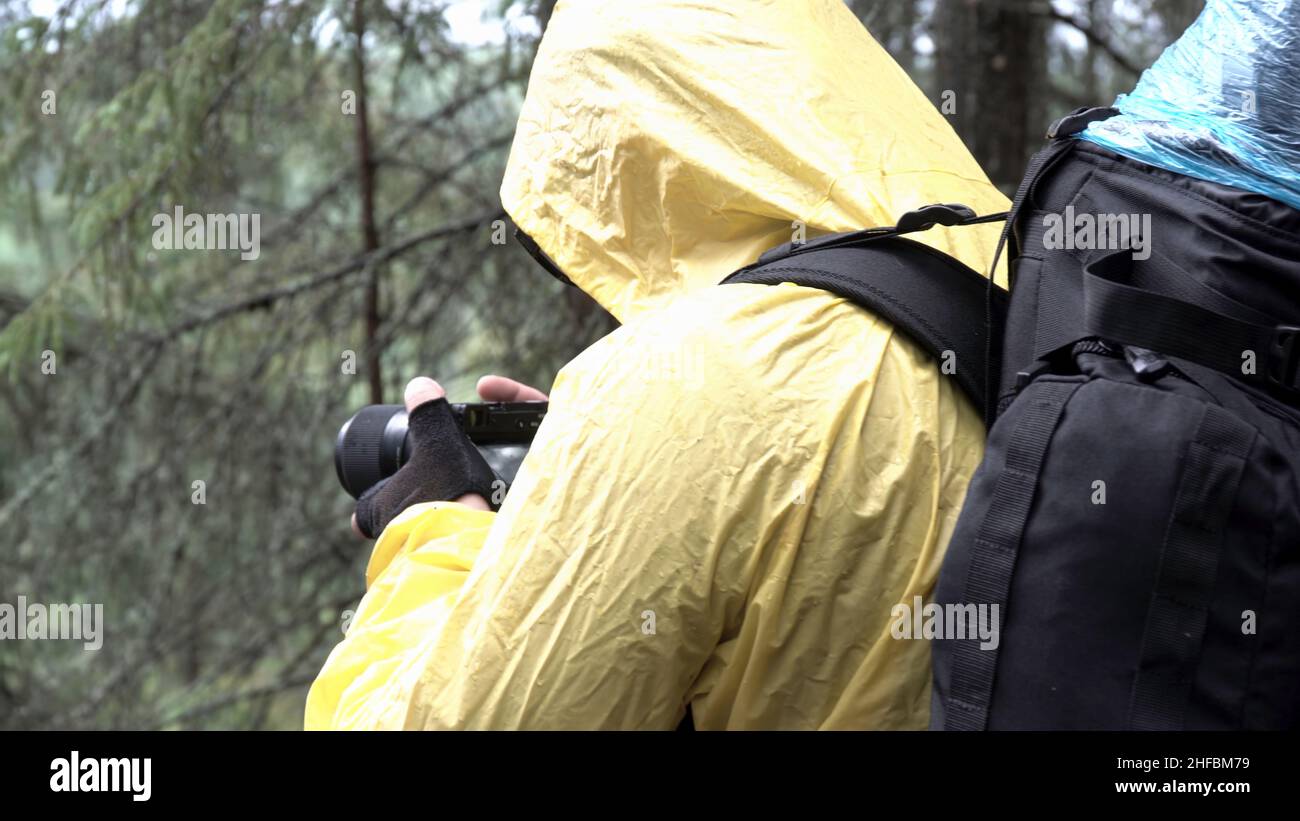 Side view of a youn man standing among trees and taking pictures of ...