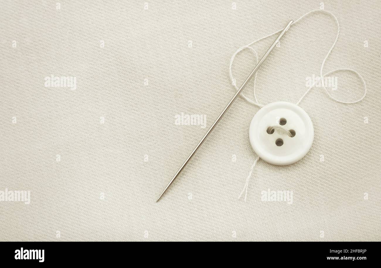 The needle and thread lie on a white cloth. Button on clothes ...