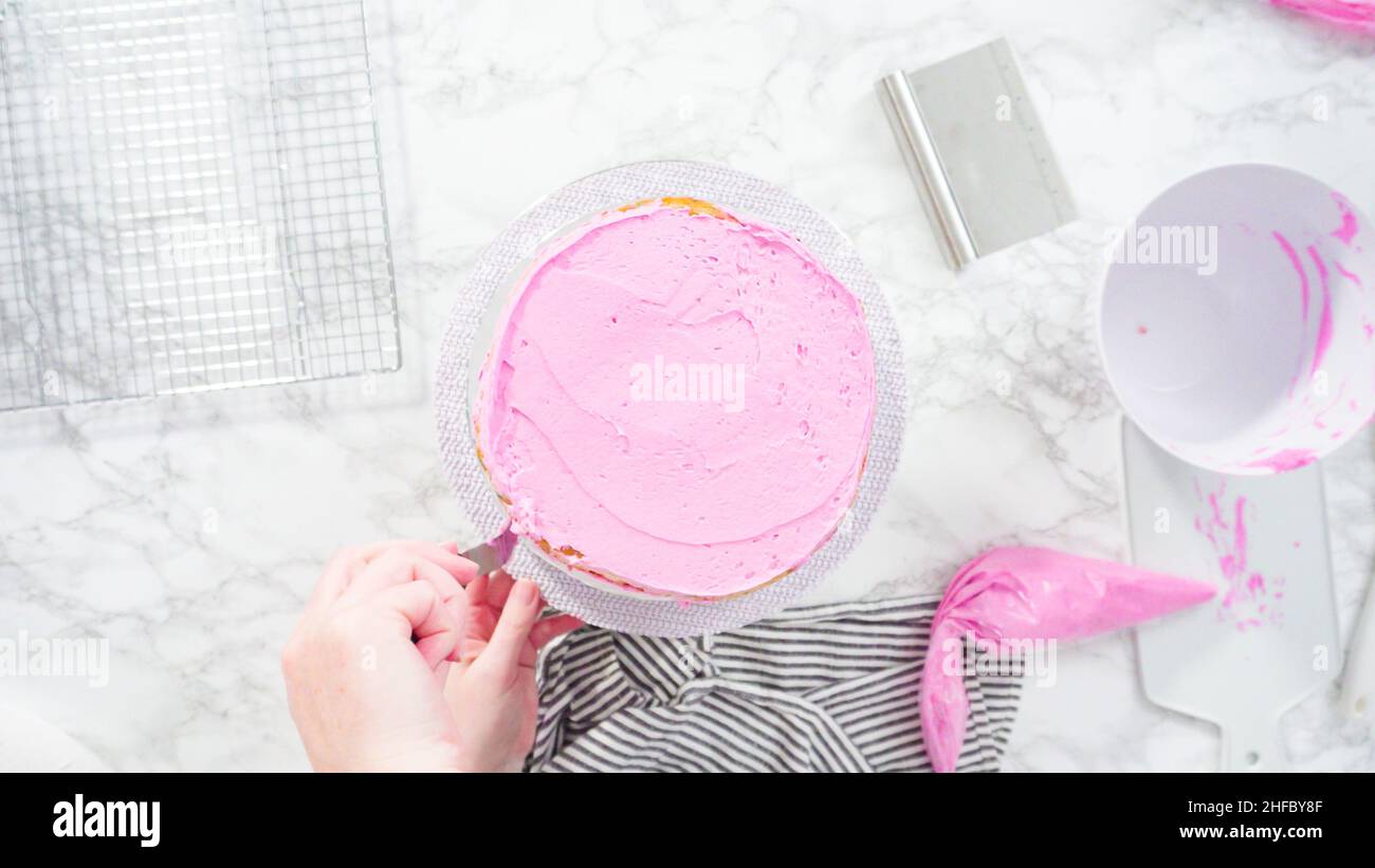 Flat lay. Step by step. Frosting round funfetti cake layers with pink ...