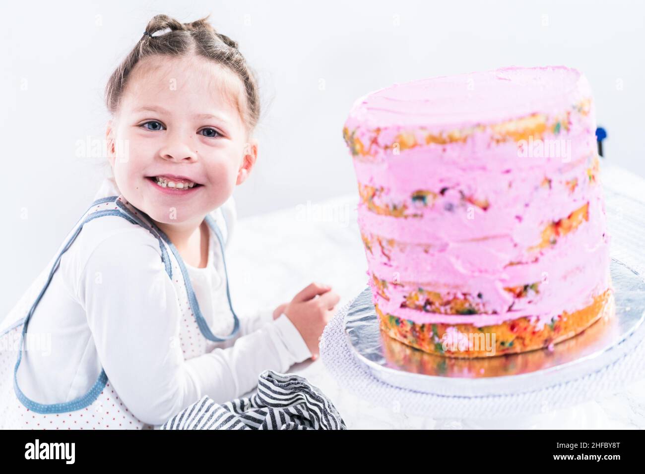 Little girl helping to bake tall funfetti cake with pink buttercream ...