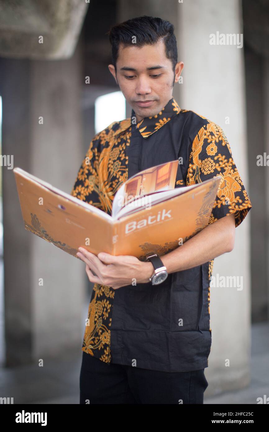 A young male model dressed in Indonesian Batik is reading a book ...