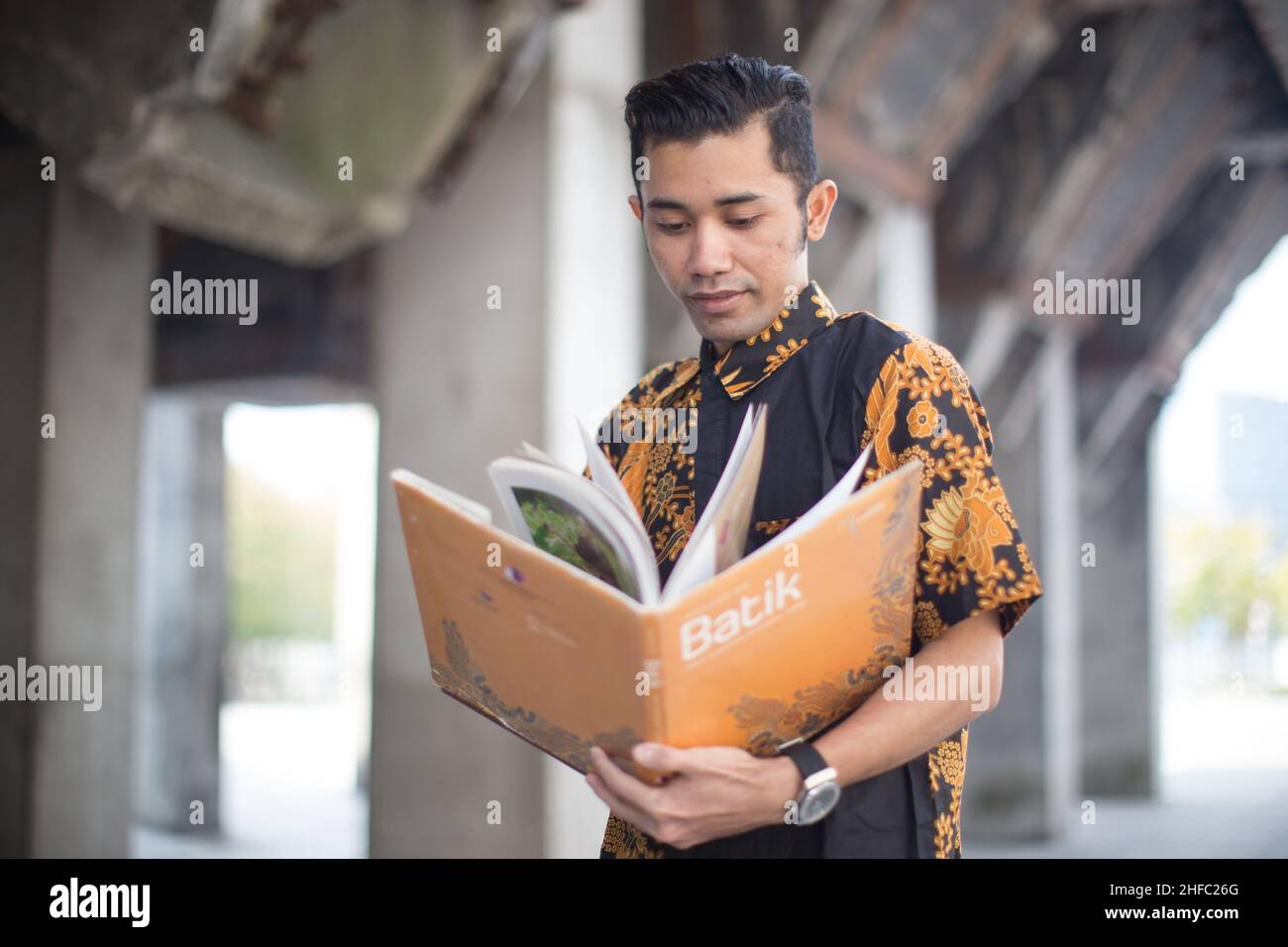 A young male model dressed in Indonesian Batik is reading a book ...