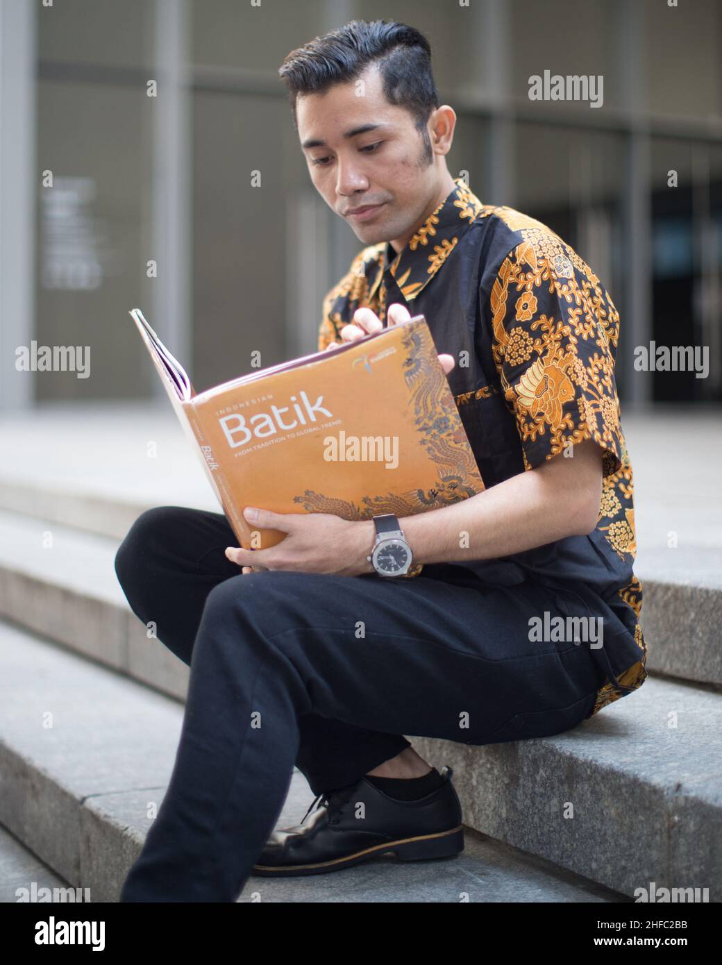 A young male model dressed in Indonesian Batik is reading a book ...