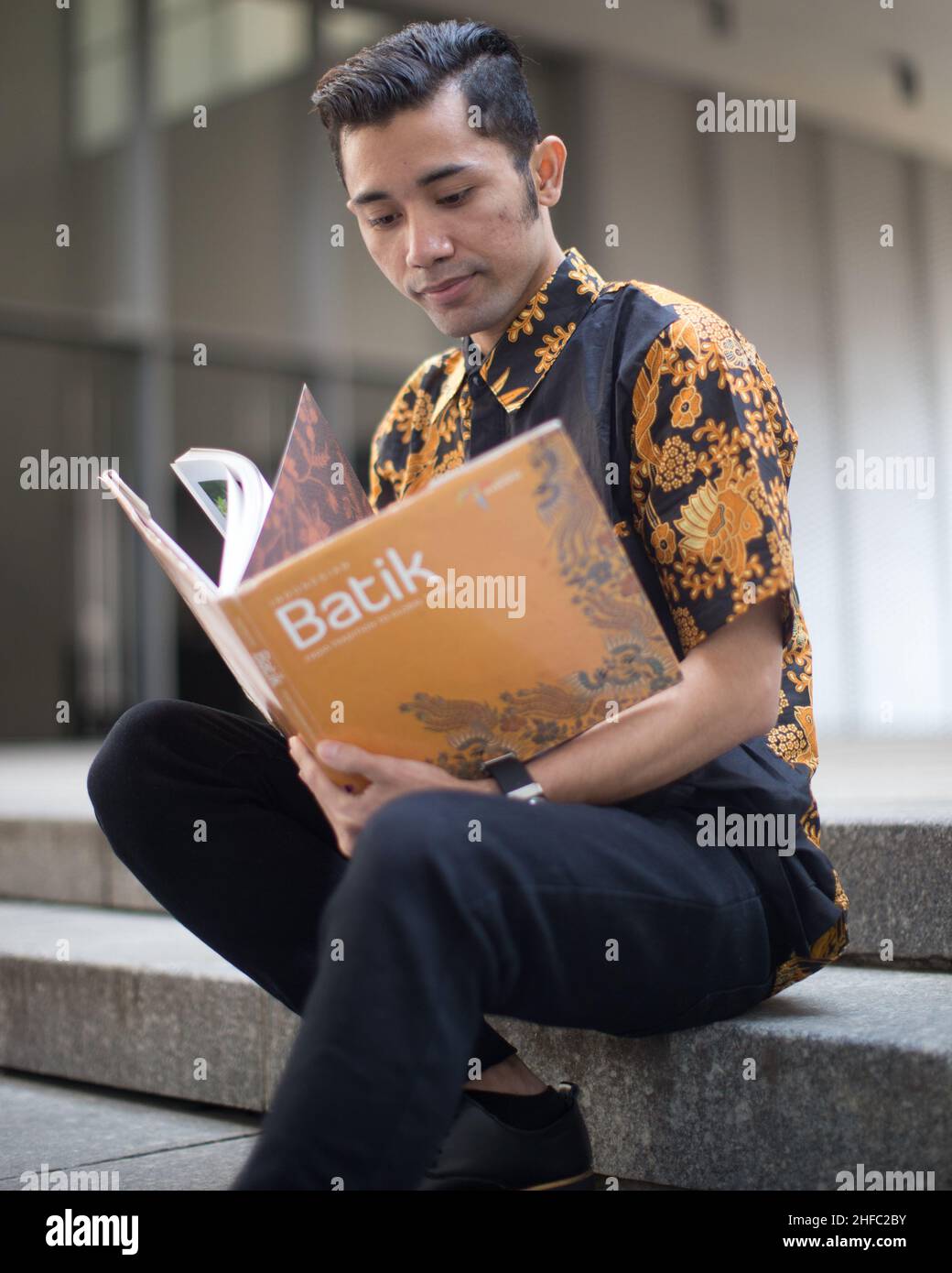 A young male model dressed in Indonesian Batik is reading a book ...