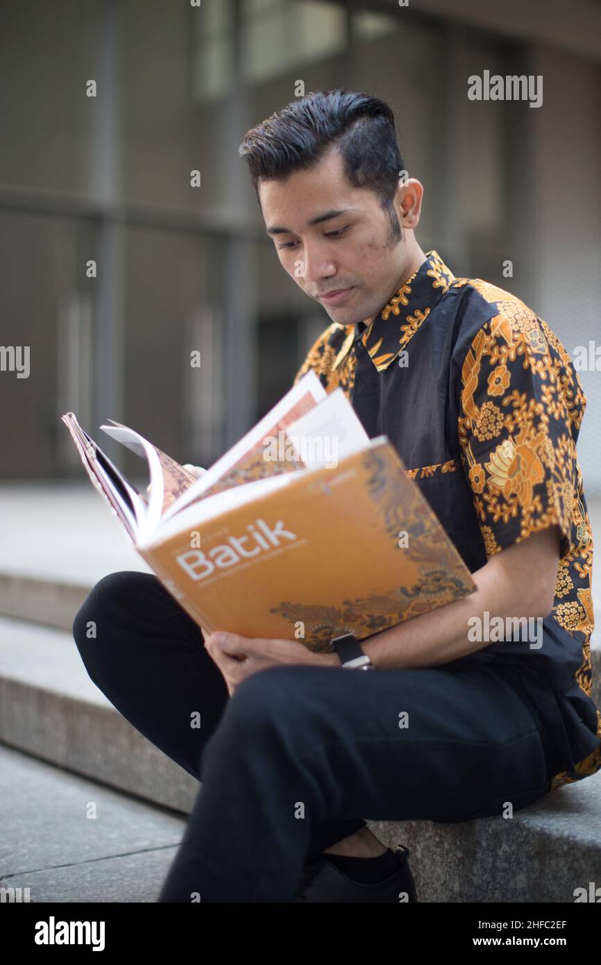 A young male model dressed in Indonesian Batik is reading a book ...