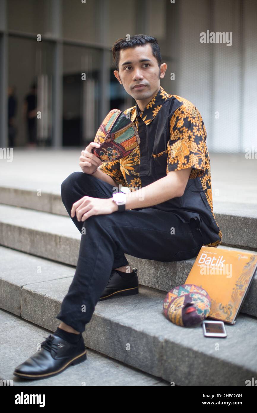 A young male model dressed in Indonesian Batik sits holding a Javanese ...