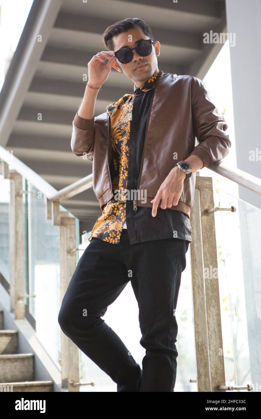 A young male model dressed in stylish Indonesian Batik holds sunglasses ...