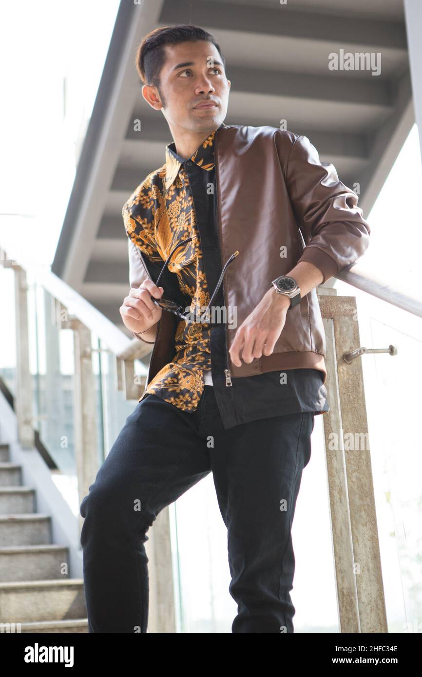 A young male model dressed in stylish Indonesian Batik holds sunglasses ...