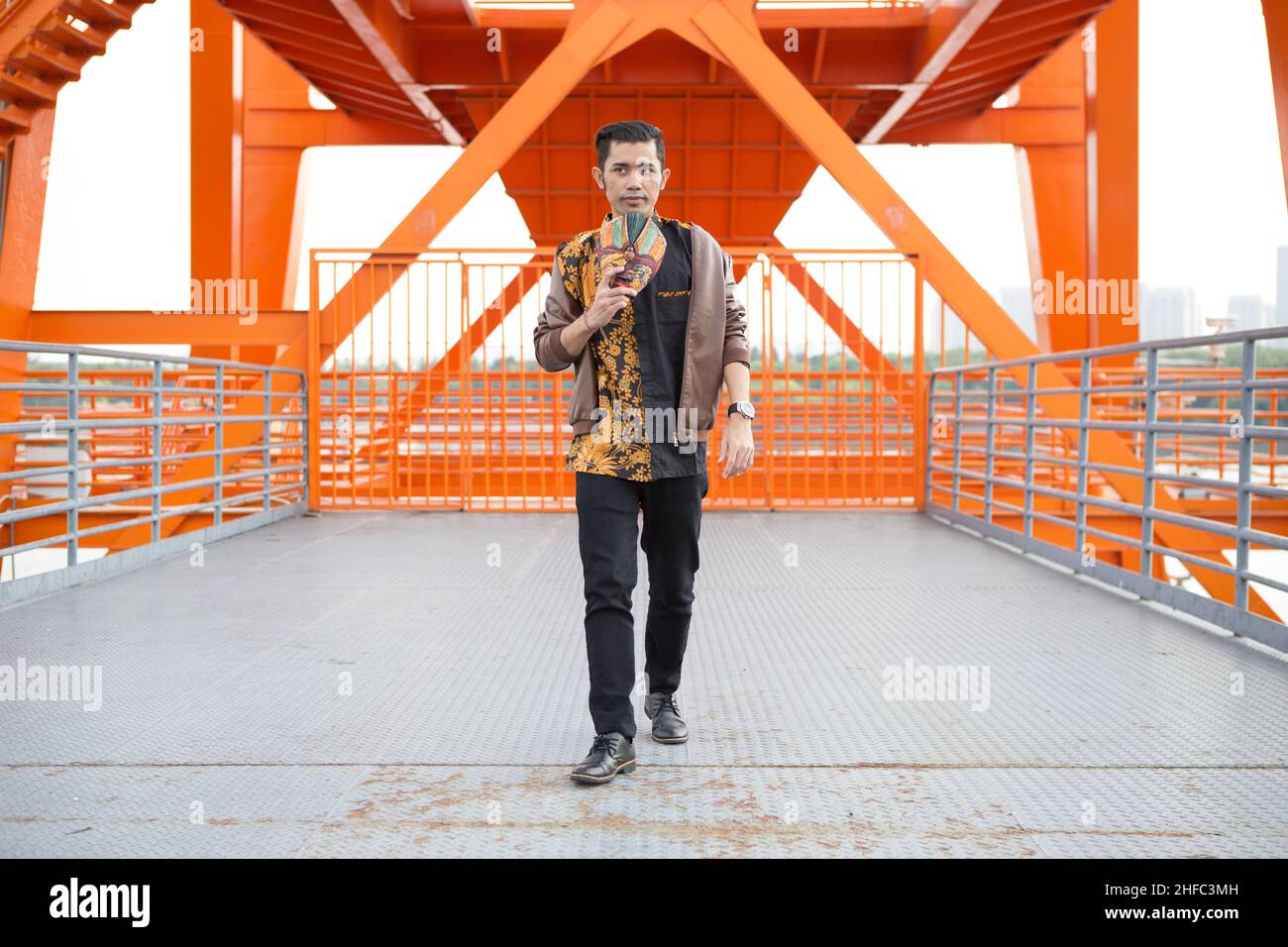 A young male model dressed in Indonesian Batik holds a Javanese mask ...