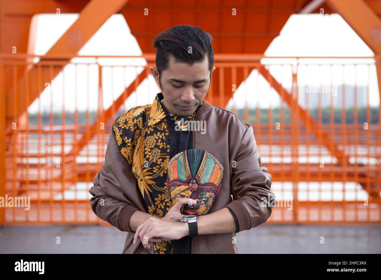 A young male model dressed in Indonesian Batik holds a Javanese mask ...